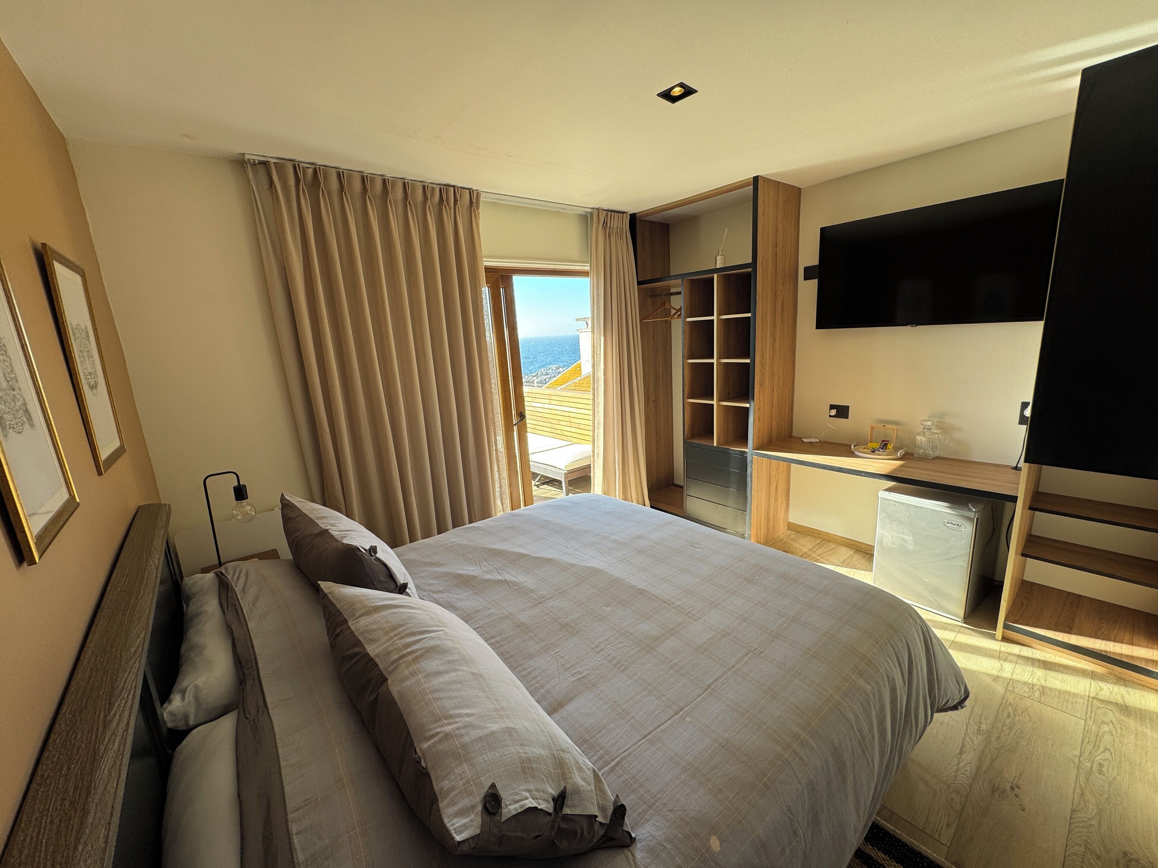 Quarto de hotel com uma cama grande, uma escrivaninha com computador, televisão e vista para o mar.