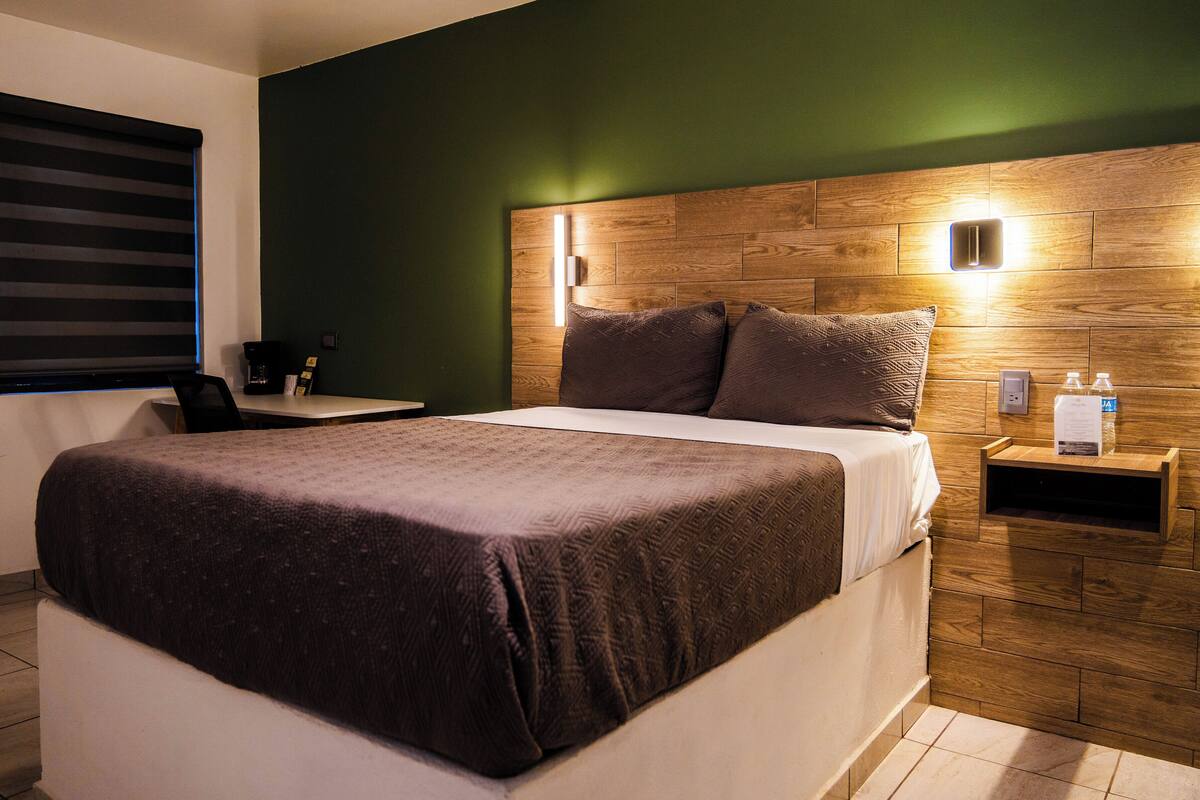 Quarto de hotel moderno com uma cama grande, uma mesa de cabeceira e uma luminária fixada na parede.