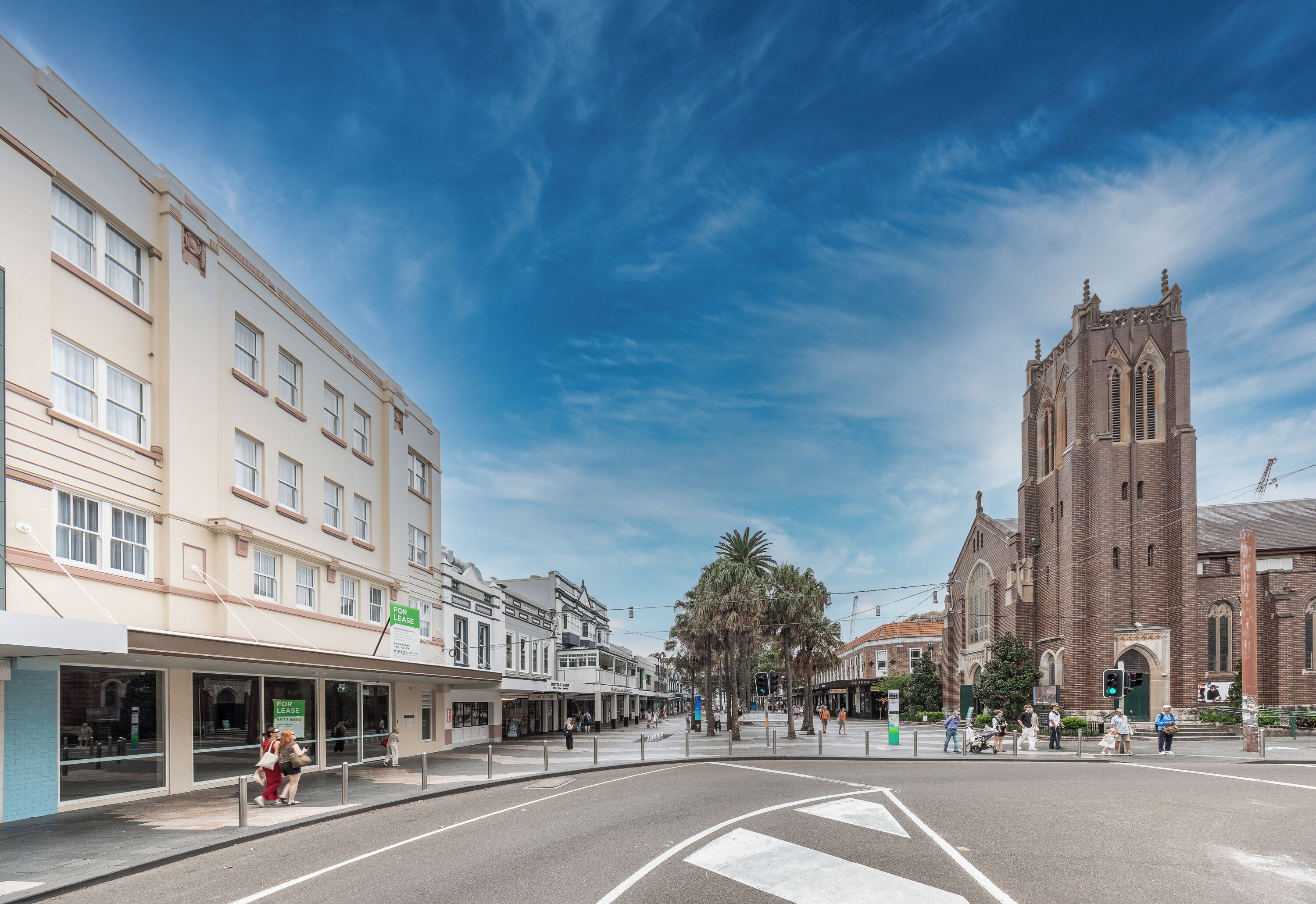 Uma rua com uma igreja, lojas e uma faixa de pedestres.