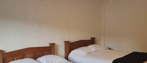 Quarto com duas camas de madeira, um ventilador de teto e um candeeiro.