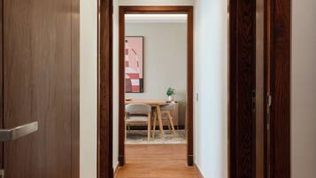 Corredor que dá para uma sala de jantar, com chão de madeira, mesa, duas cadeiras e um vaso com planta.