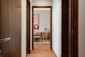 Corredor que dá para uma sala de jantar, com chão de madeira, mesa, duas cadeiras e um vaso com planta.