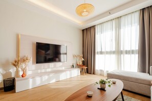 Uma sala de estar moderna com televisão de tela plana, um sofá, uma mesa de centro e uma janela grande com cortinas.