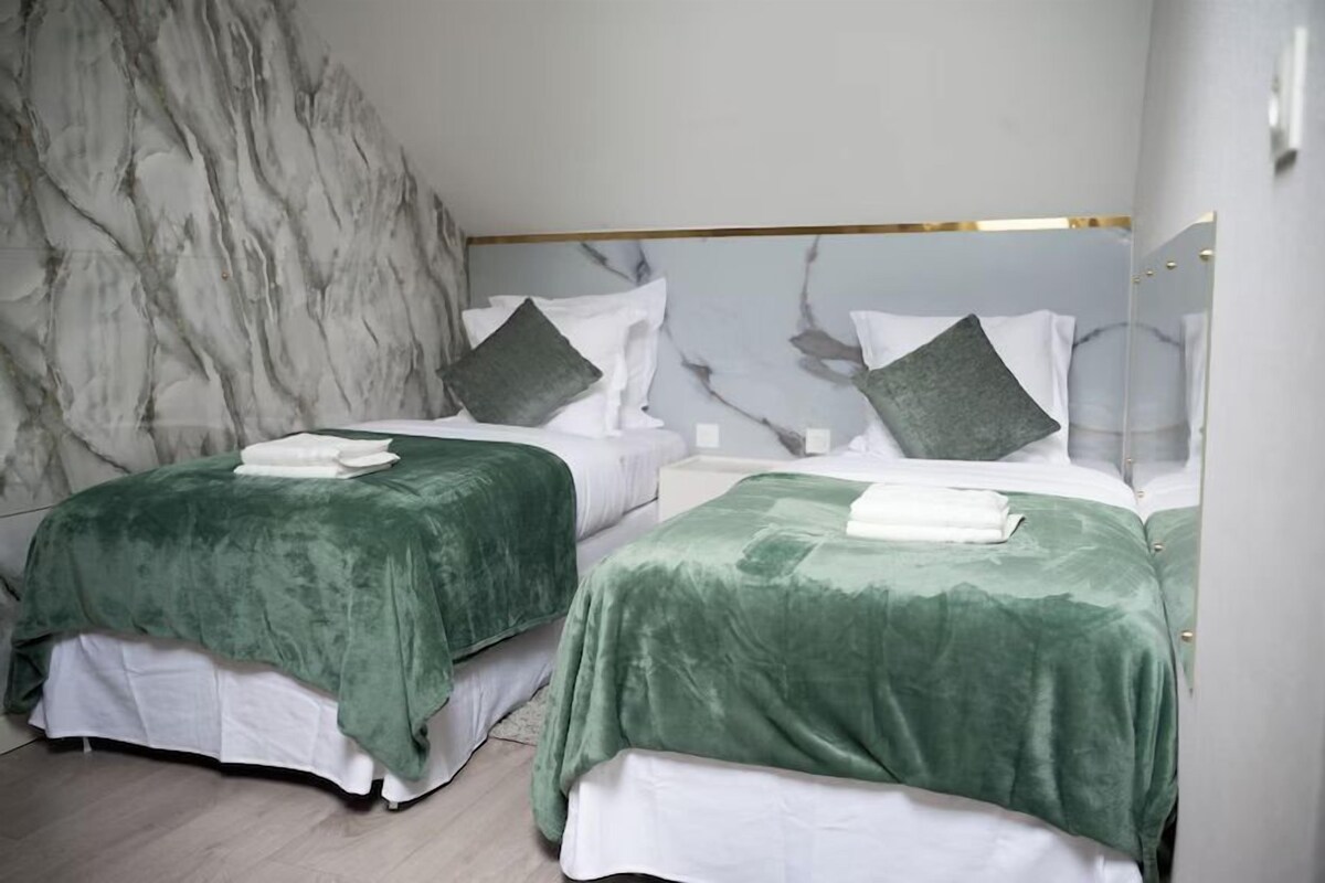 Quarto de hotel com duas camas, parede de mármore e design moderno.