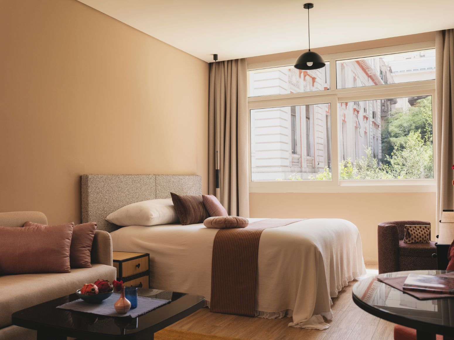 Quarto de hotel com uma cama, um sofá, uma mesinha e uma janela com vista para edifícios.