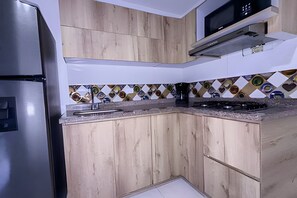 Cozinha com armários de madeira, geladeira de aço inoxidável, micro-ondas e painel de azulejos.