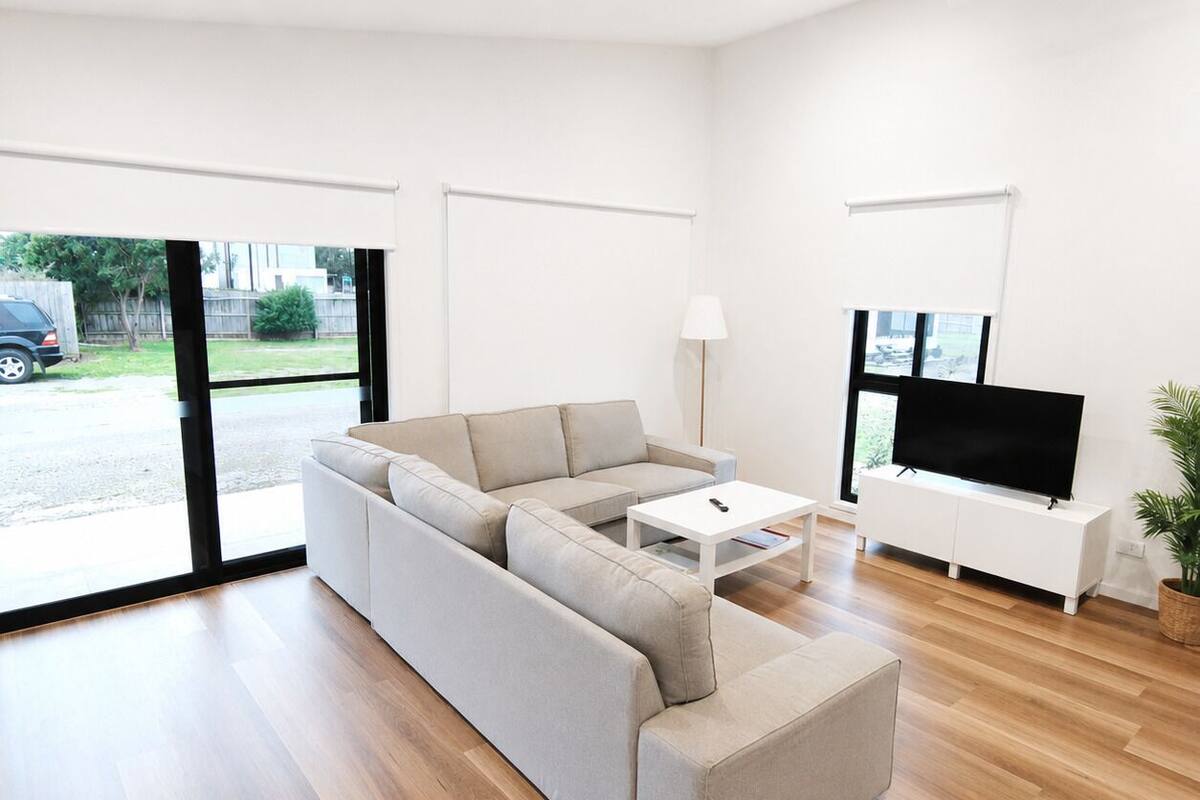 Uma sala de estar moderna com um sofá seccional, uma mesa de centro, uma TV em um suporte branco e um ventilador de teto.