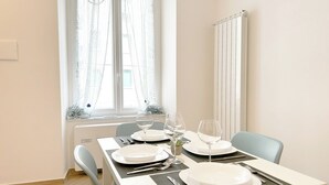 Uma área de refeições com uma mesa posta para quatro pessoas, um radiador e uma janela com cortinas.