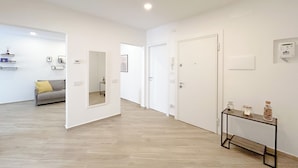 Interior moderno com piso de madeira, sofá com almofada amarela, espelho e mesa com objetos decorativos.