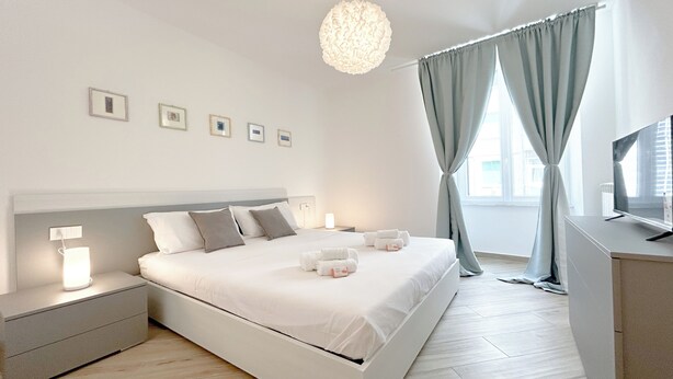 Quarto moderno com cama, abajures, televisão e cortinas.
