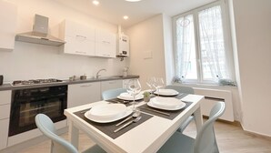 Uma cozinha moderna com armários brancos, fogão a gás e área de refeições para quatro pessoas, com mesa, cadeiras e janela com vista.
