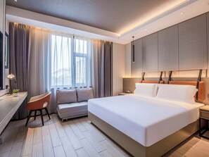 Quarto de hotel moderno com uma cama grande, uma escrivaninha e um espaço de estar confortável.
