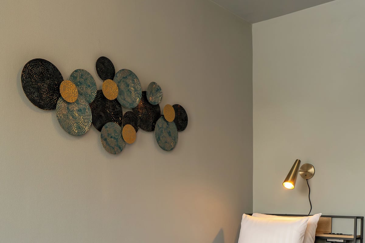 Quarto moderno com estrutura de cama preta, roupa de cama branca e uma obra de arte na parede acima da cama.