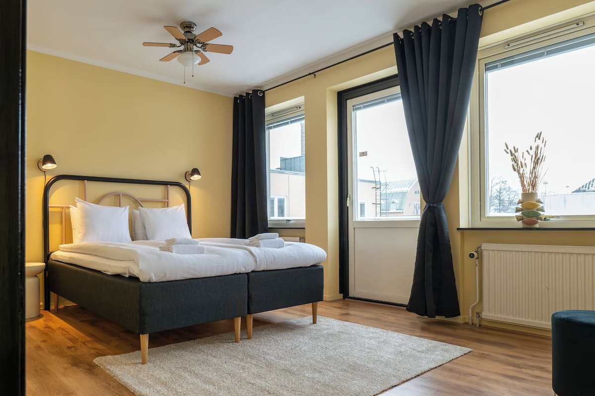Quarto com cama, ventoinha no teto, janela com cortinas e radiador.