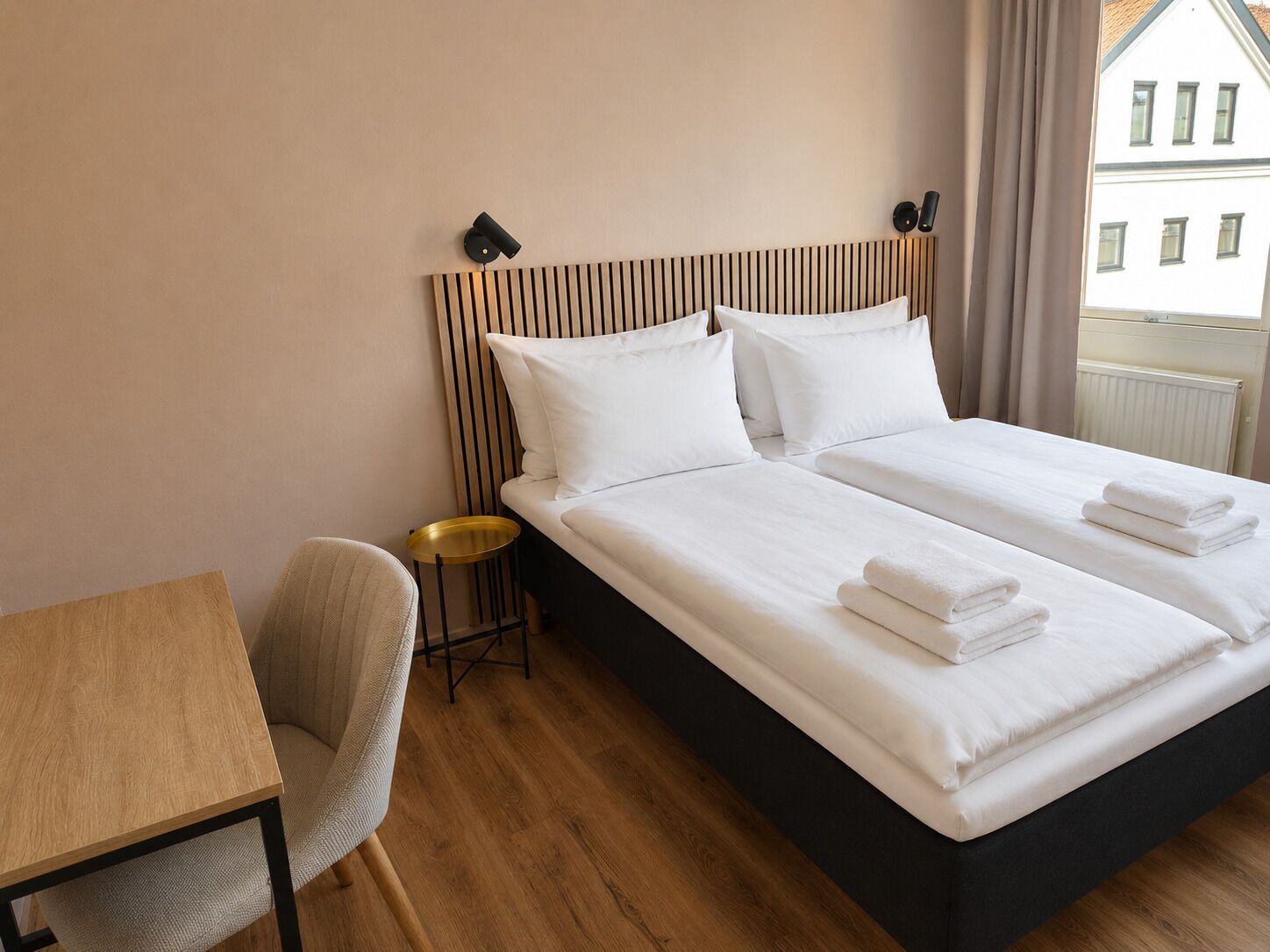 Quarto de hotel com cama, uma pequena mesa, uma cadeira e vista para edifícios.