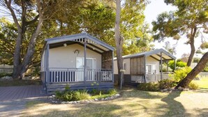 Duas casas móveis com decks e grades de madeira, rodeadas por árvores e um caminho pavimentado.