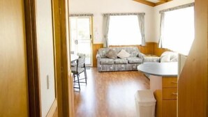 Um corredor com piso de madeira e vigas aparentes, que leva a uma sala de estar com sofá e mesa.