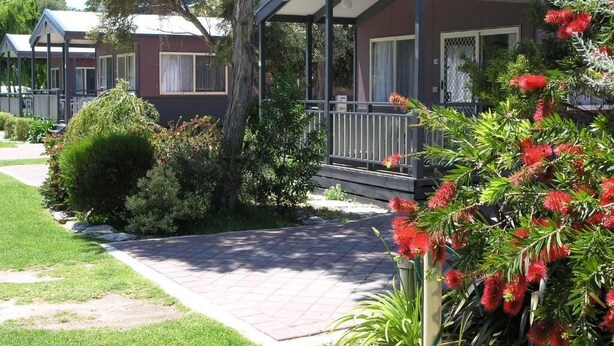 Fileira de casas móveis com varanda coberta, rodeadas por jardins bem cuidados e plantas floridas.