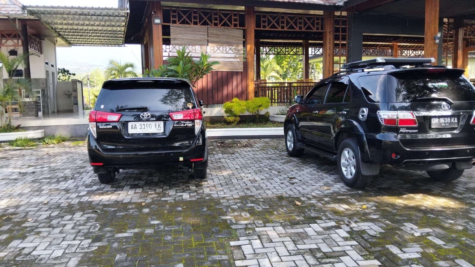 Dois carros estacionados em frente a um edifício com calçada de ladrilhos e estrutura de madeira.