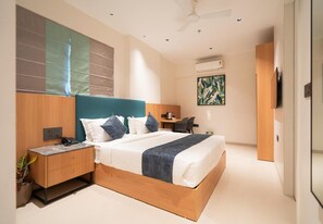 Quarto de hotel moderno com uma cama grande, uma mesa de cabeceira, uma escrivaninha e uma cadeira.