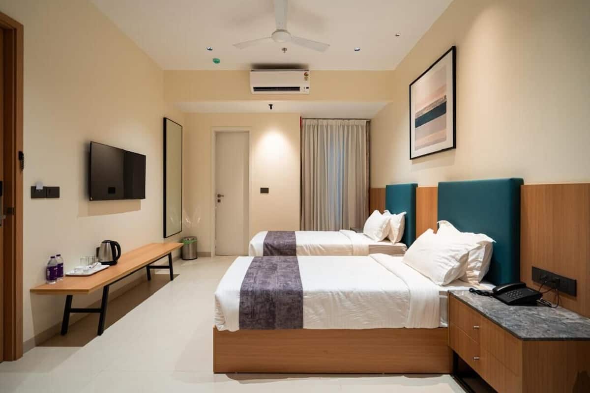 Quarto de hotel com duas camas, uma escrivaninha, televisão e ventoinha no teto.