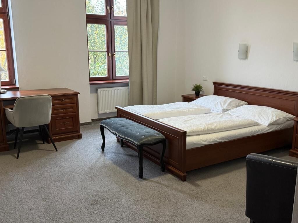 Quarto com cama de madeira, escrivaninha, cadeira e radiador.