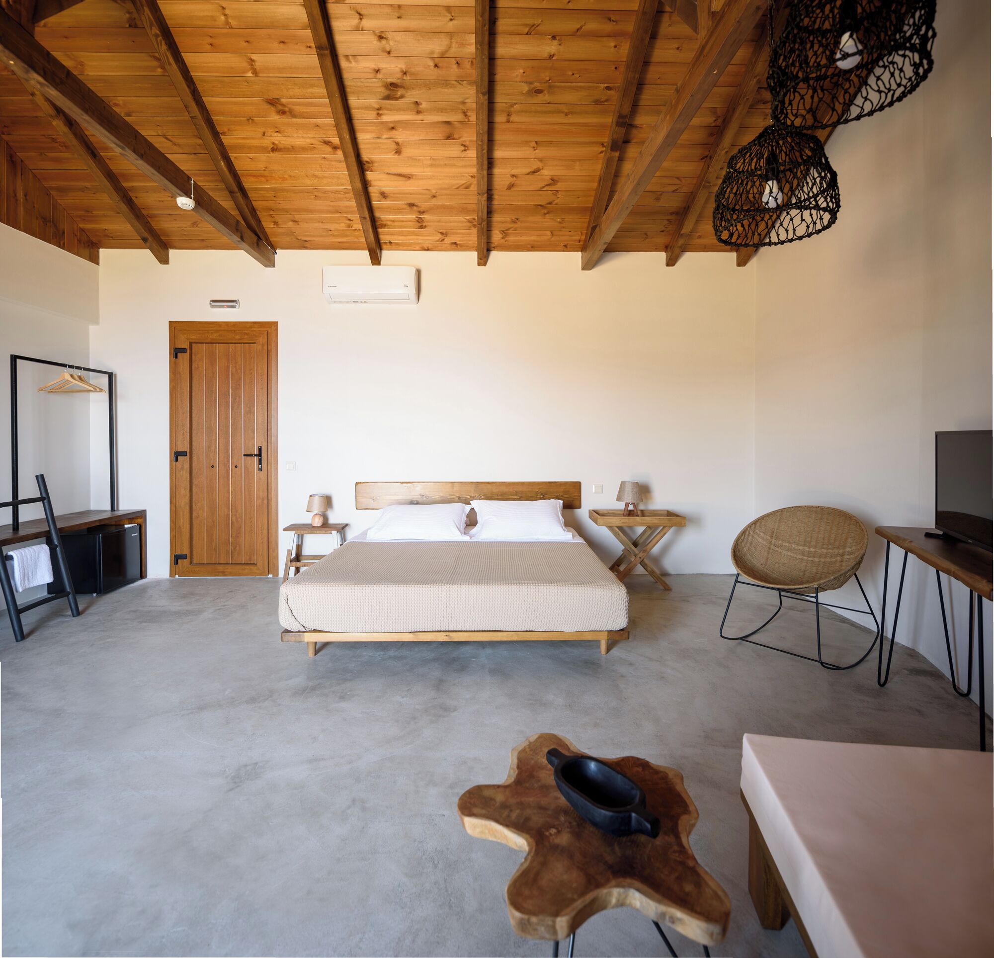 Quarto com teto de madeira, cama, escrivaninha, cadeira e uma pequena mesa com uma tigela.