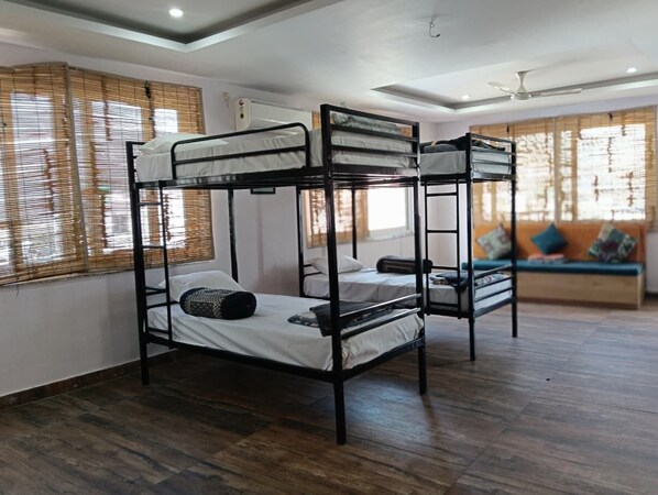 Quarto com beliches, piso de madeira, sofá com almofadas e ventoinha no teto.