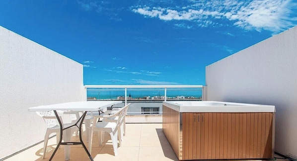 Terraço no telhado com mesa e cadeiras, uma banheira de hidromassagem e vista para o horizonte da cidade.