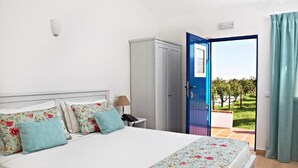 Quarto com cama, mesa de cabeceira, guarda-roupa e vista para um jardim através de uma porta aberta.