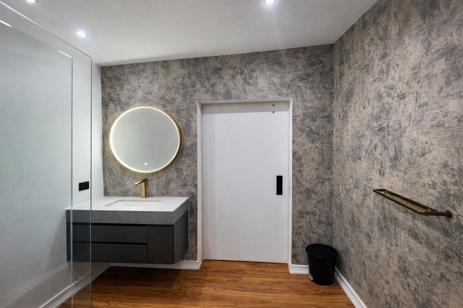 Casa de banho moderna com espelho redondo, lavatório branco e porta com puxador.