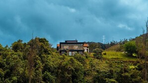 Uma casa moderna com telhado plano, rodeada por vegetação densa e um céu nublado.