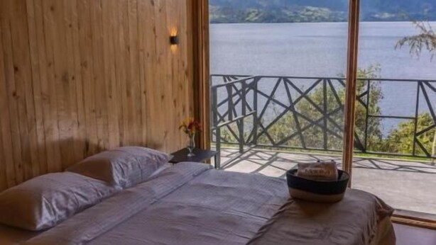 Quarto com painéis de madeira, duas camas, vista para um lago e montanhas, e varanda com guarda-corpo.