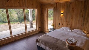 Quarto com painéis de madeira, uma cama grande, uma mesinha de cabeceira e janela com vista para o exterior.