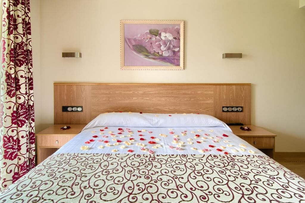 Cama bem arrumada com colcha estampada, cabeceira de madeira, mesas de cabeceira com abajures e uma obra de arte floral emoldurada na parede.