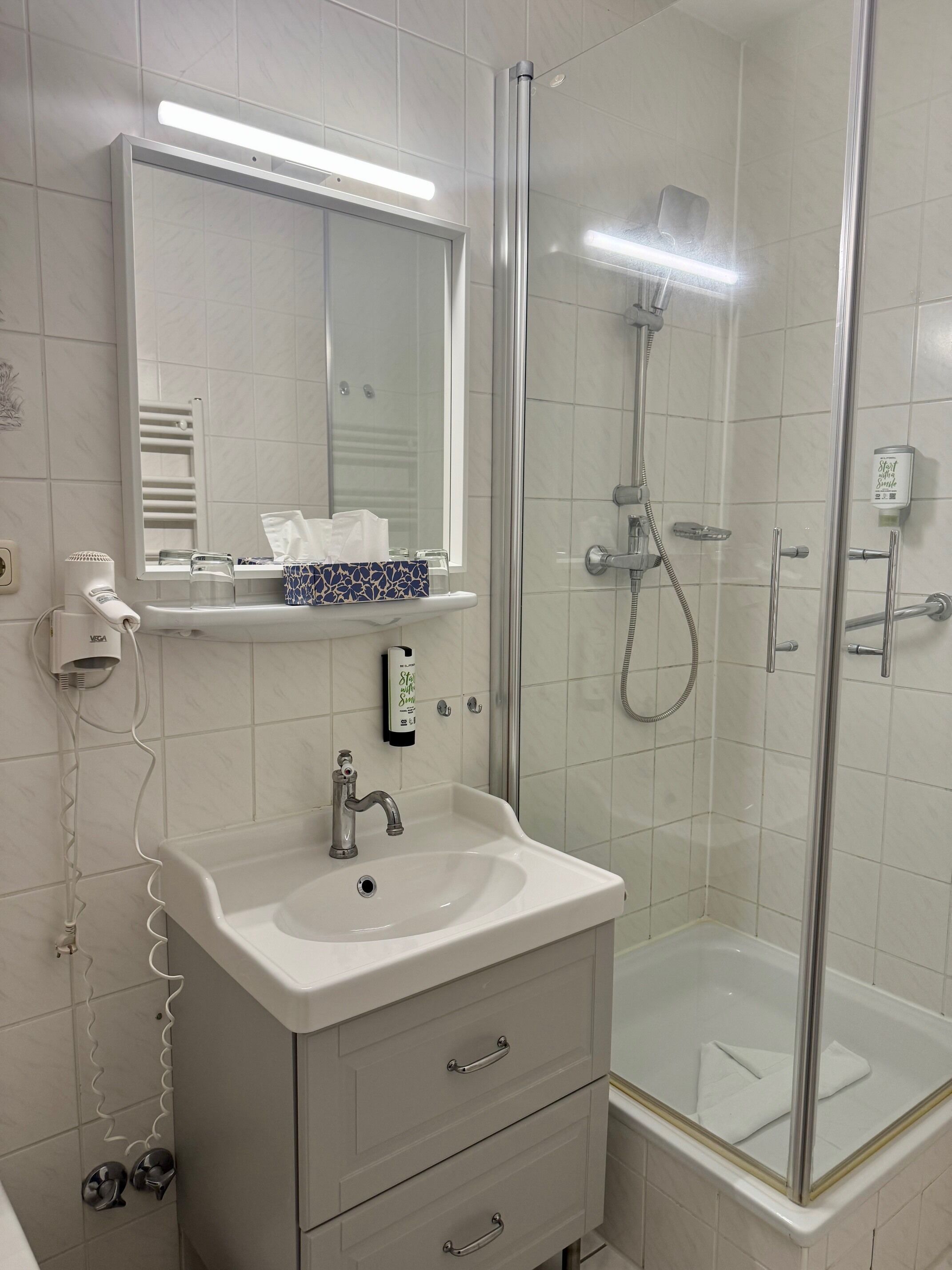 Casa de banho com lavatório branco, espelho e cabine de duche em vidro.