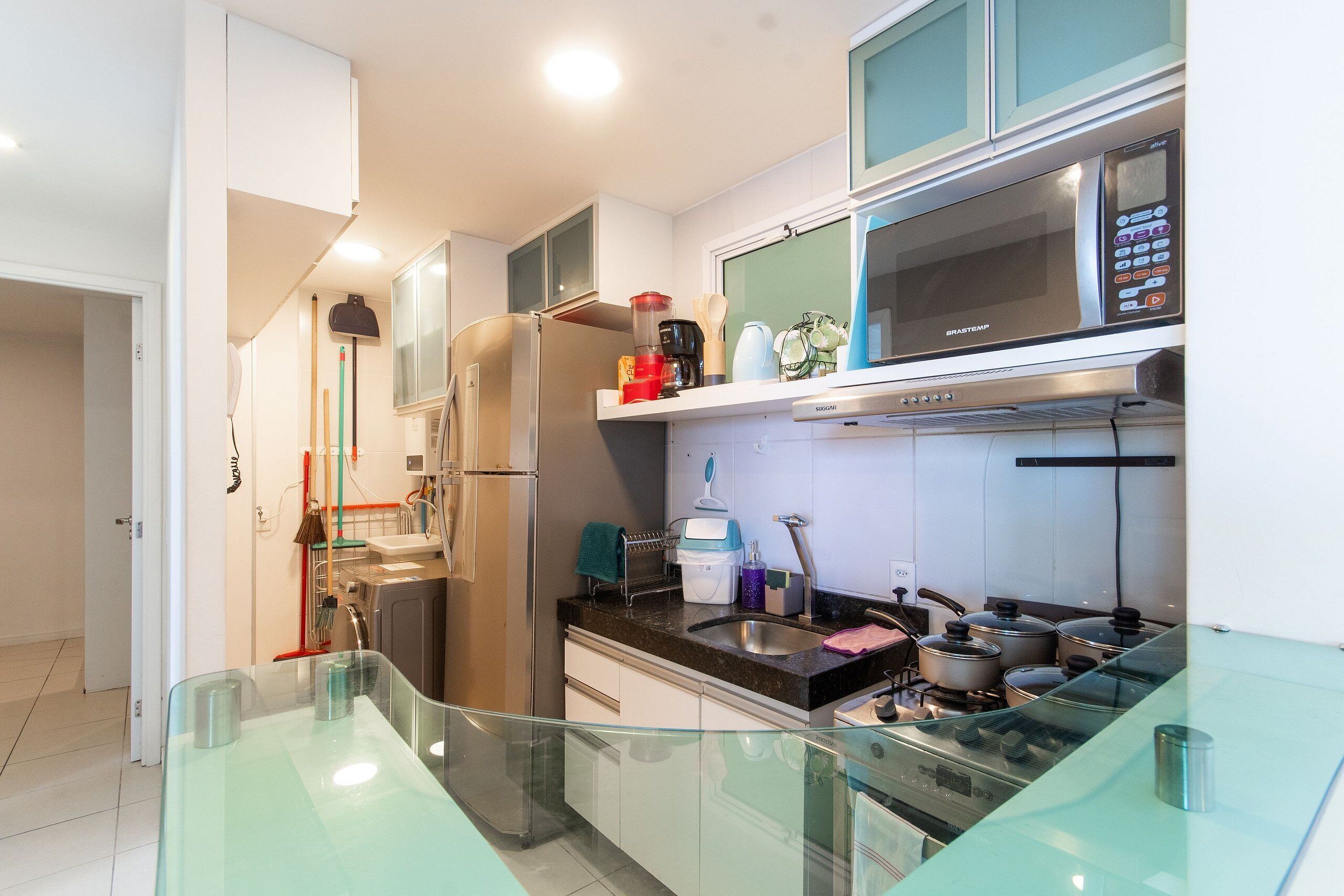 Uma cozinha moderna com geladeira de aço inoxidável, micro-ondas e bancada em vidro.