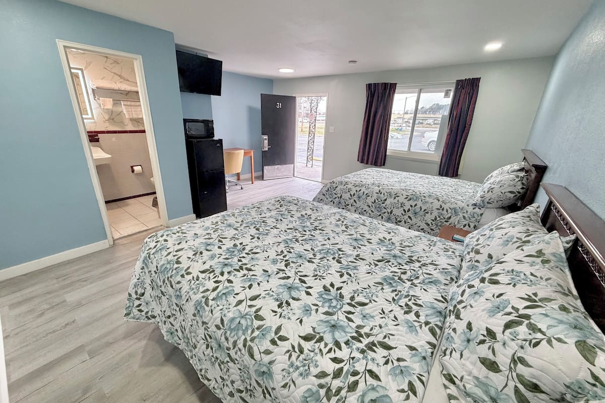 Quarto de hotel com duas camas, televisão, pequena escrivaninha e banheiro visível por uma porta aberta.