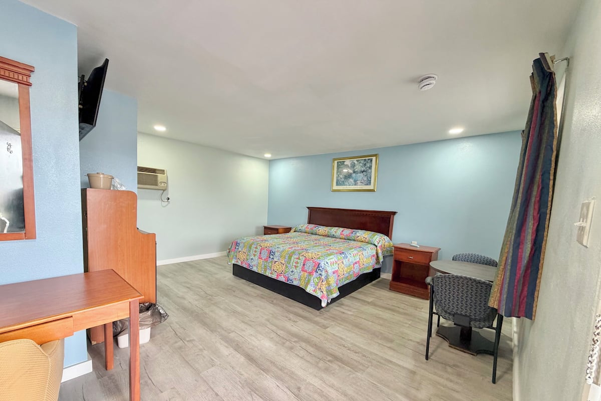 Quarto de hotel com cama, mesas de cabeceira, escrivaninha, cadeira, espelho e um quadro na parede.