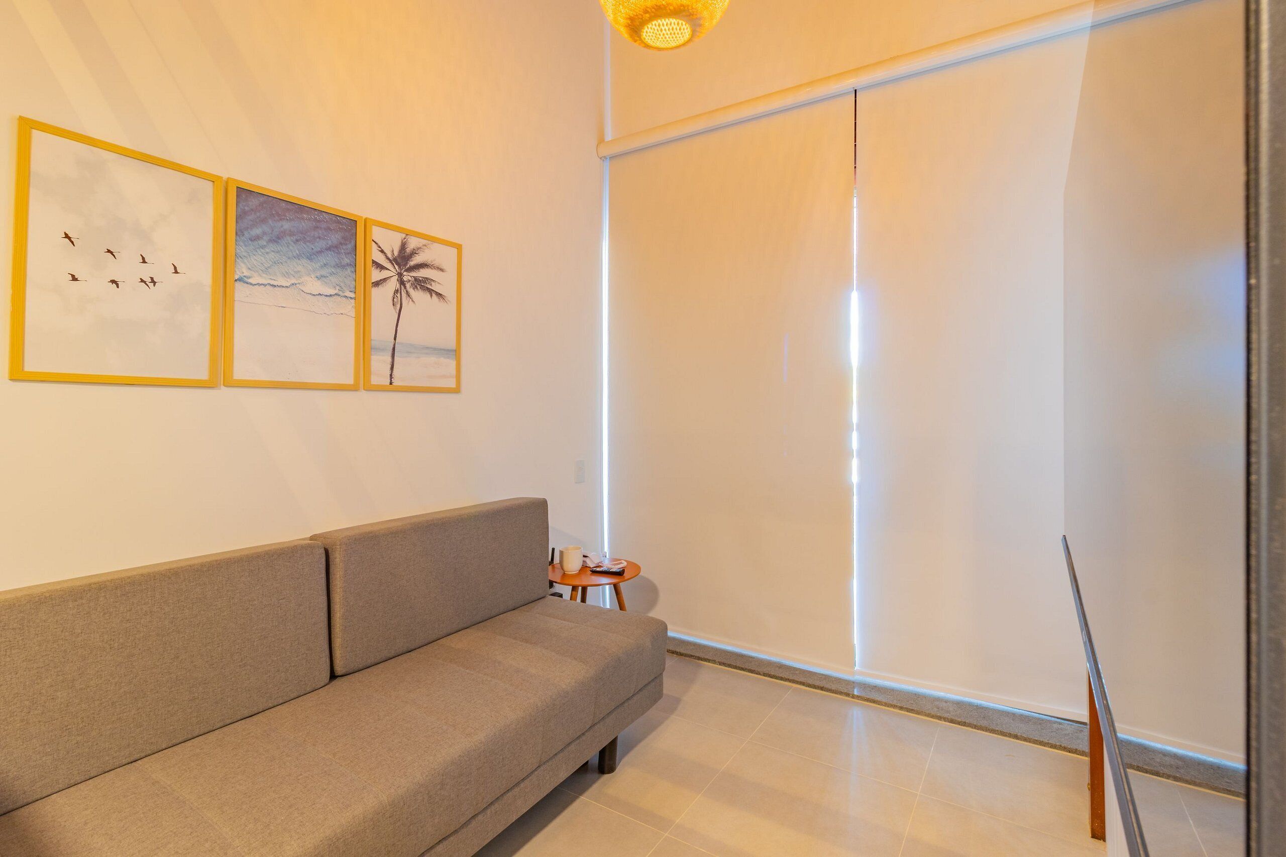 Uma sala de estar moderna com um sofá, uma mesa redonda pequena e três obras de arte emolduradas na parede.