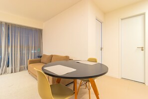 Uma sala de estar moderna com uma mesa redonda preta, um sofá bege e uma cadeira amarela.