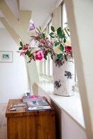 Uma mesa de madeira com revistas e um vaso de flores num parapeito.