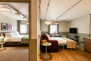 Quarto de hotel com cama, escrivaninha, cadeira, televisão e janela.