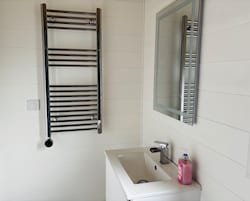 Casa de banho com lavatório branco, espelho e suporte para toalhas.