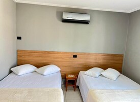 Quarto de hotel com duas camas de solteiro, cabeceira de madeira, mesa de cabeceira pequena em madeira e ar-condicionado fixado na parede.
