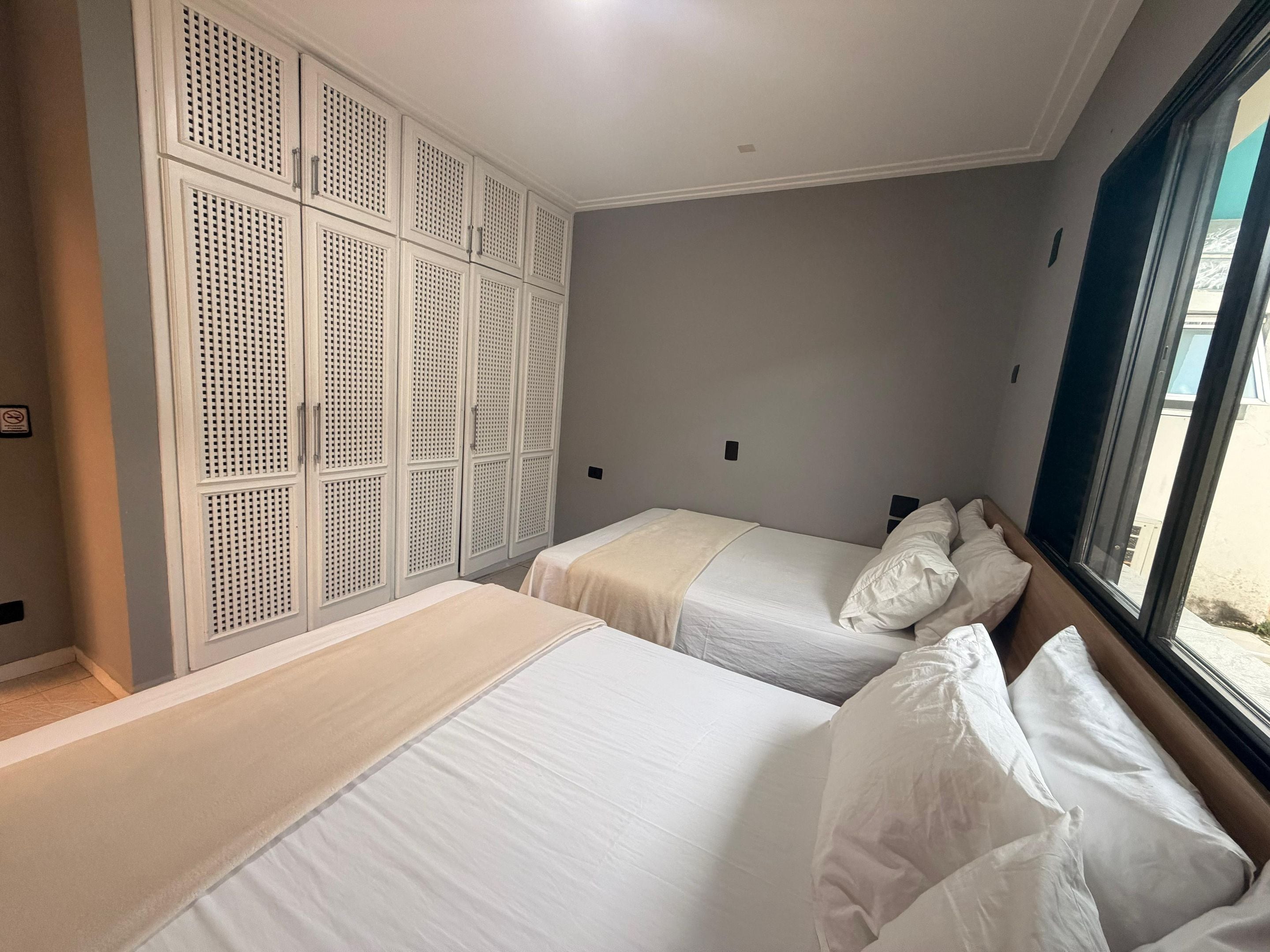 Quarto com duas camas, um guarda-roupa grande e uma janela.