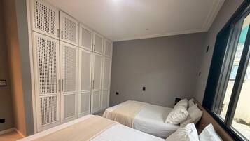 Quarto com duas camas, um guarda-roupa grande e uma janela.