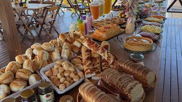 Mesa de buffet com diversos pães, doces e acompanhamentos.