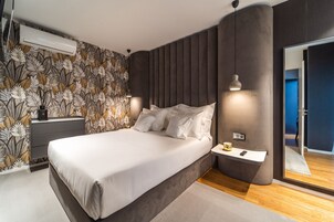 Quarto moderno com cama grande, mesa de cabeceira, espelho e ar condicionado fixado na parede.