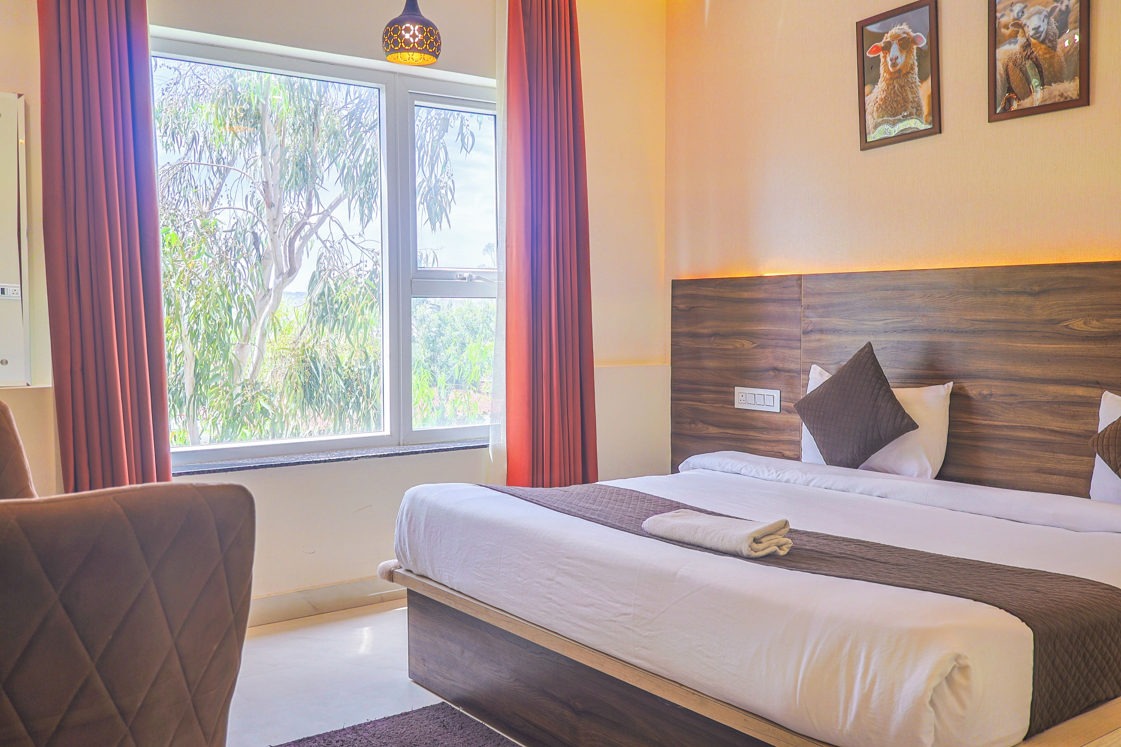 Quarto de hotel com cama, cadeira, janela com cortinas e decoração na parede.